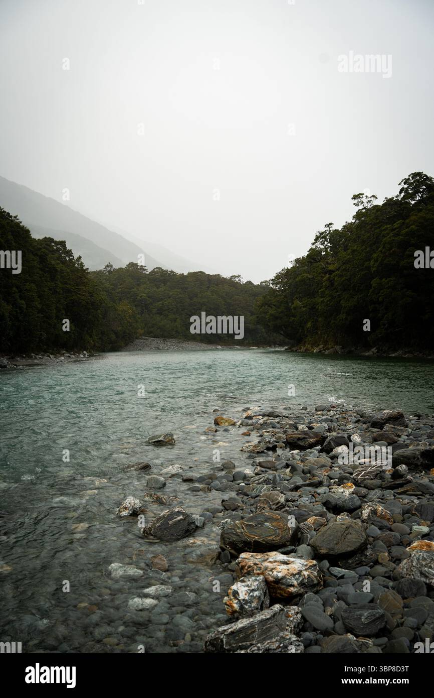 A clear, blue-green river winds through a dense, forested valley. Rocky ...