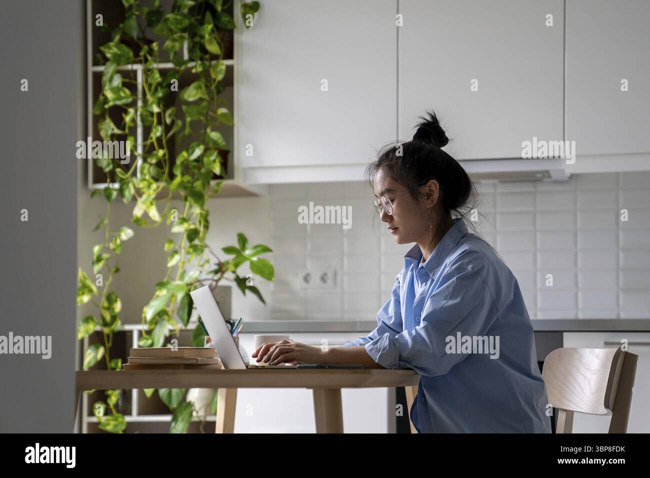 Focused Asian woman freelancer working remotely sits at table with ...