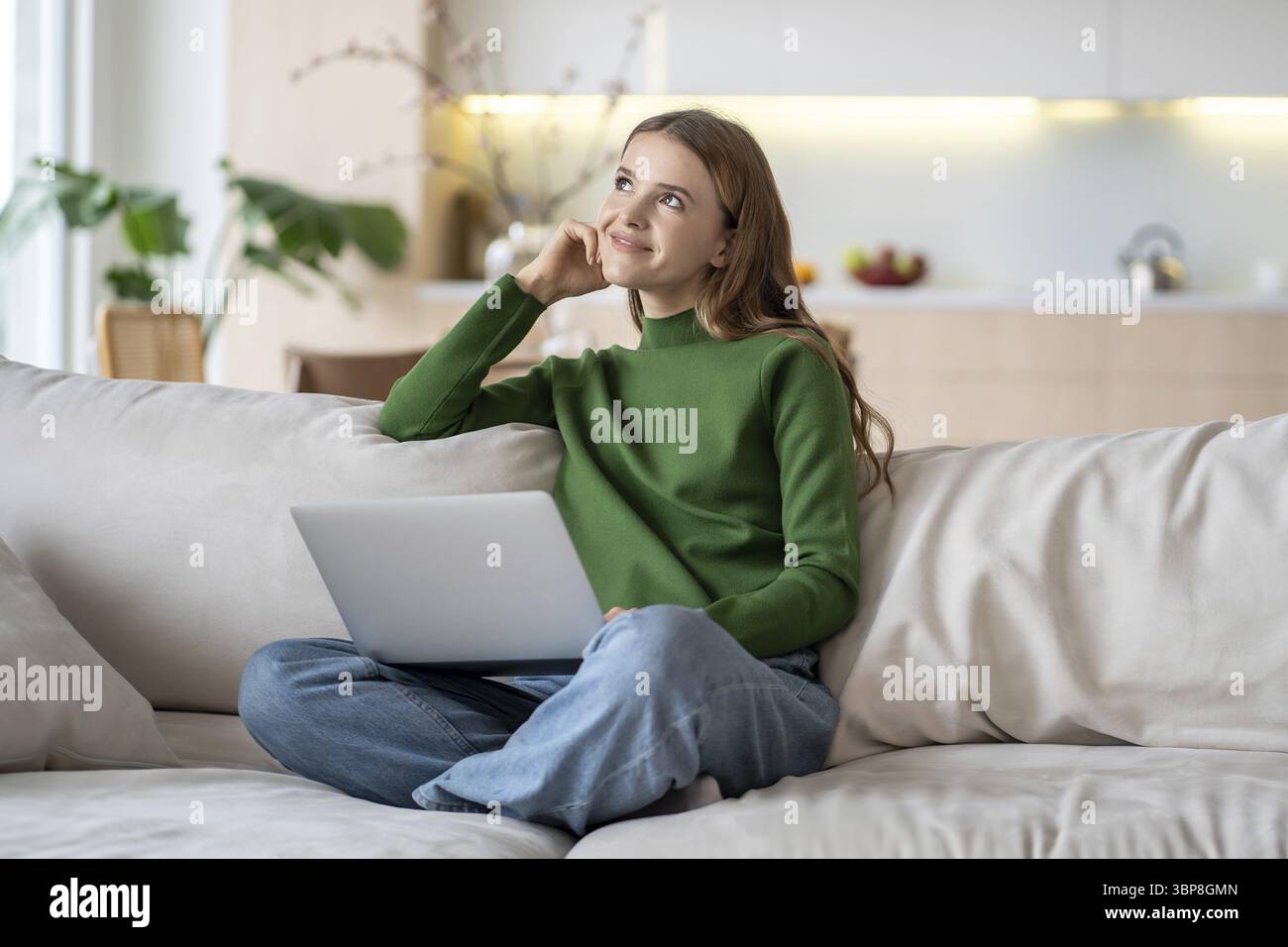 Dreamy relaxed woman sits on couch with laptop thinks about desires ...