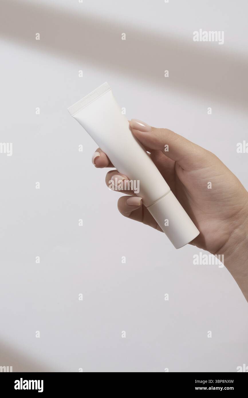 Woman's hand presents a mockup of a tube of cream. Unlabeled packaging ...
