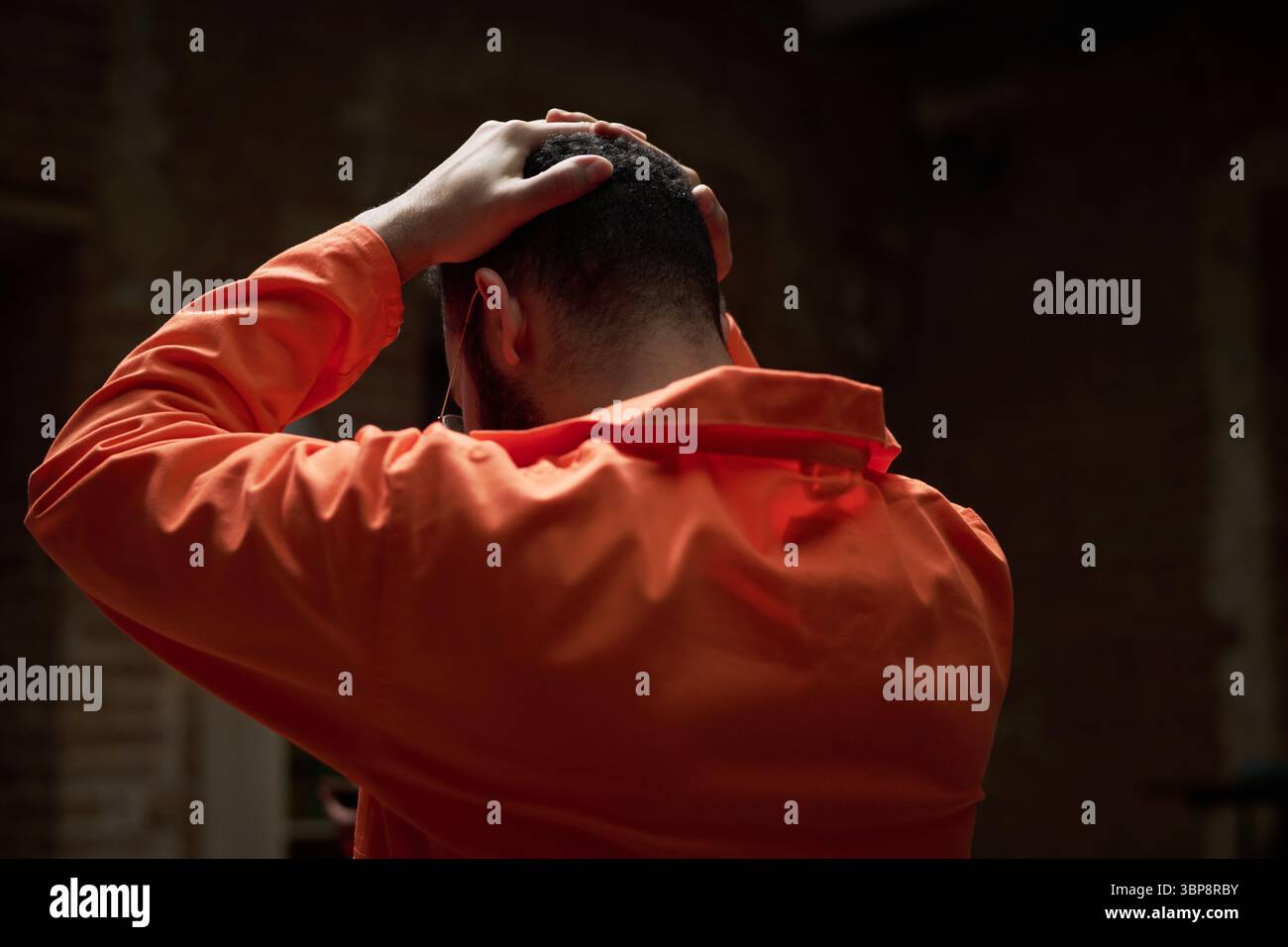 Caucasian man sitting with hands on head wearing prison uniform ...