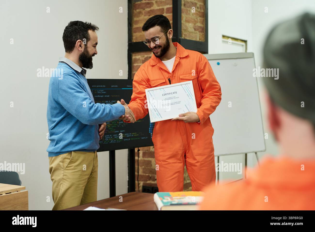 Middle aged man congratulating young adult man in orange prison uniform ...