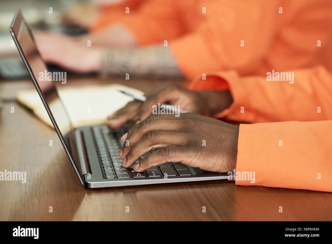 Black man wearing orange uniform typing on laptop during educational ...