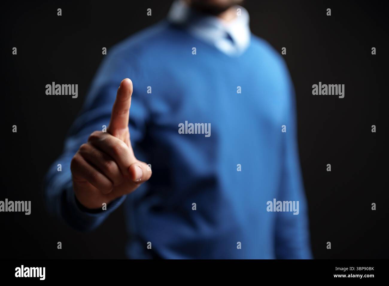 Man signaling to pause with one finger raised, dressed in casual attire ...