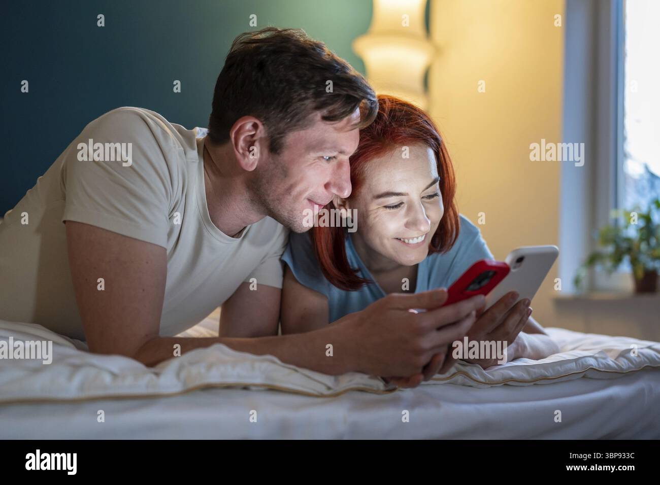 Couple looking phone while lying on bed. Girl showing boyfriend funny ...