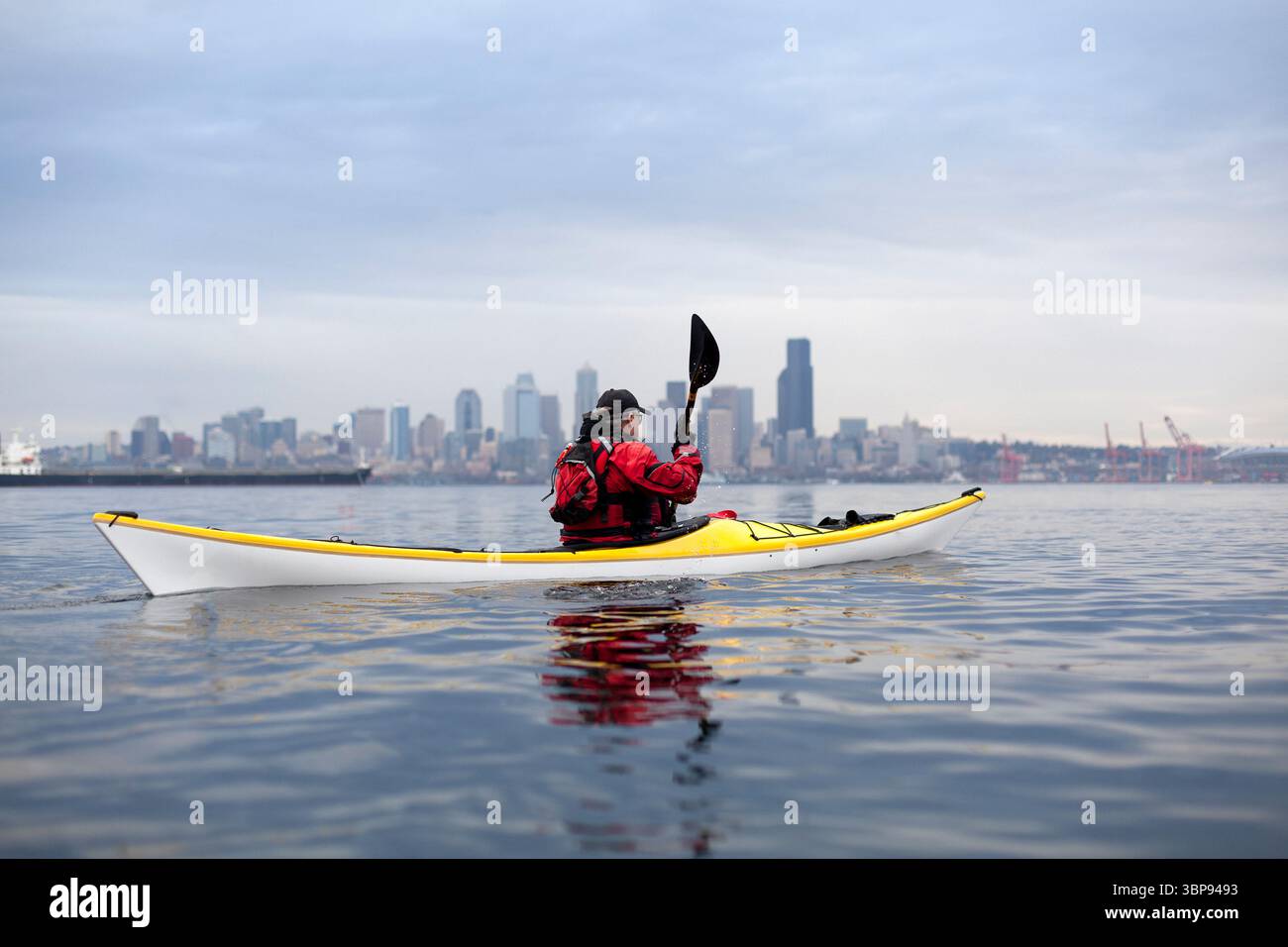 A senior male in his yellow kayak rows in front of the city skyline ...