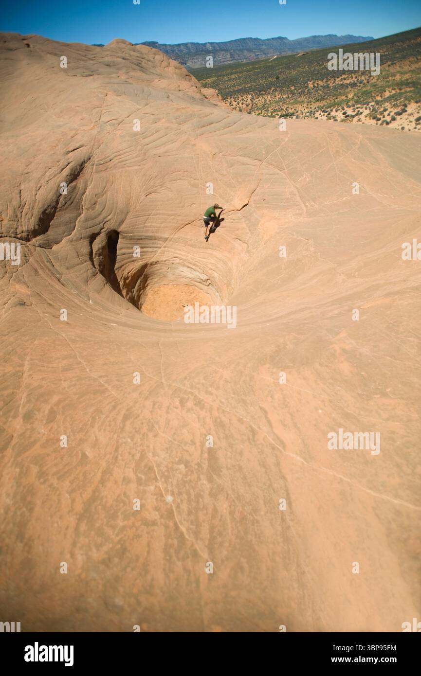 A man climbing out of a sandstone hole in Utah's Grand Staircase ...