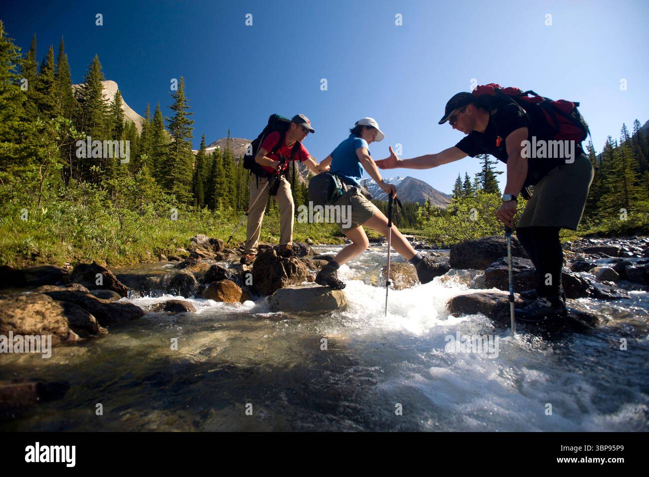 Two backpacking guides Ron Bubb and Olivier Lardin help client Julie Fisher cross a stream in ...