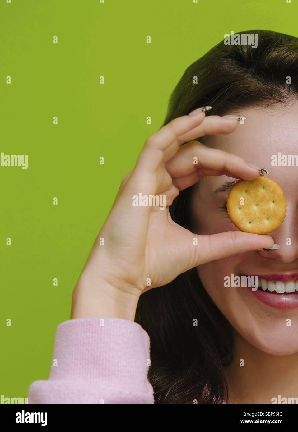 Food, Young woman is holding up a salty cracker in front of her eye and ...
