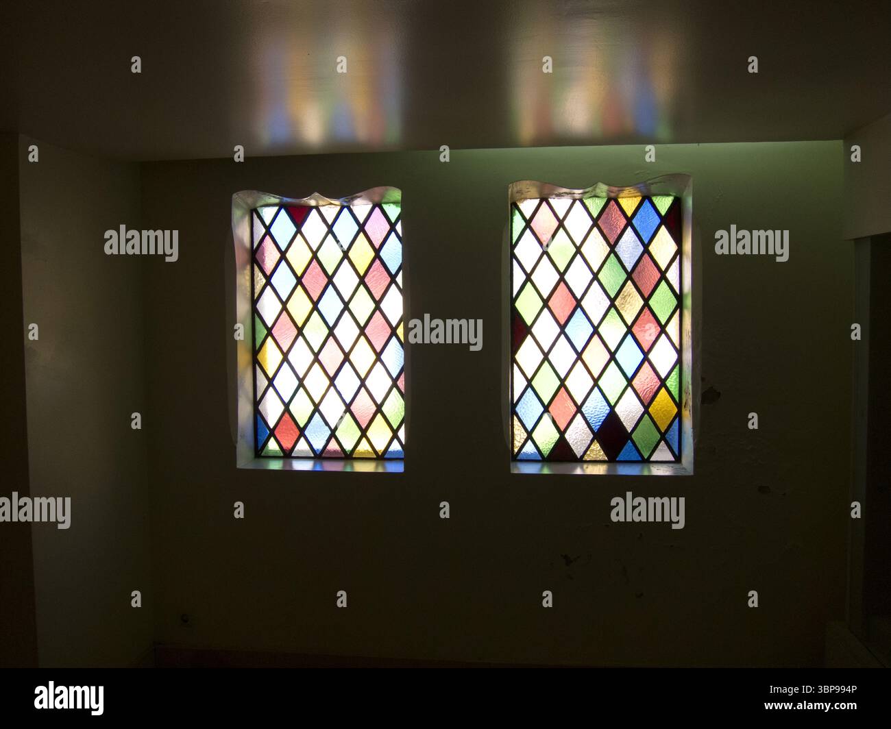 Two stained glass windows are seen in a dark room, with light shining ...