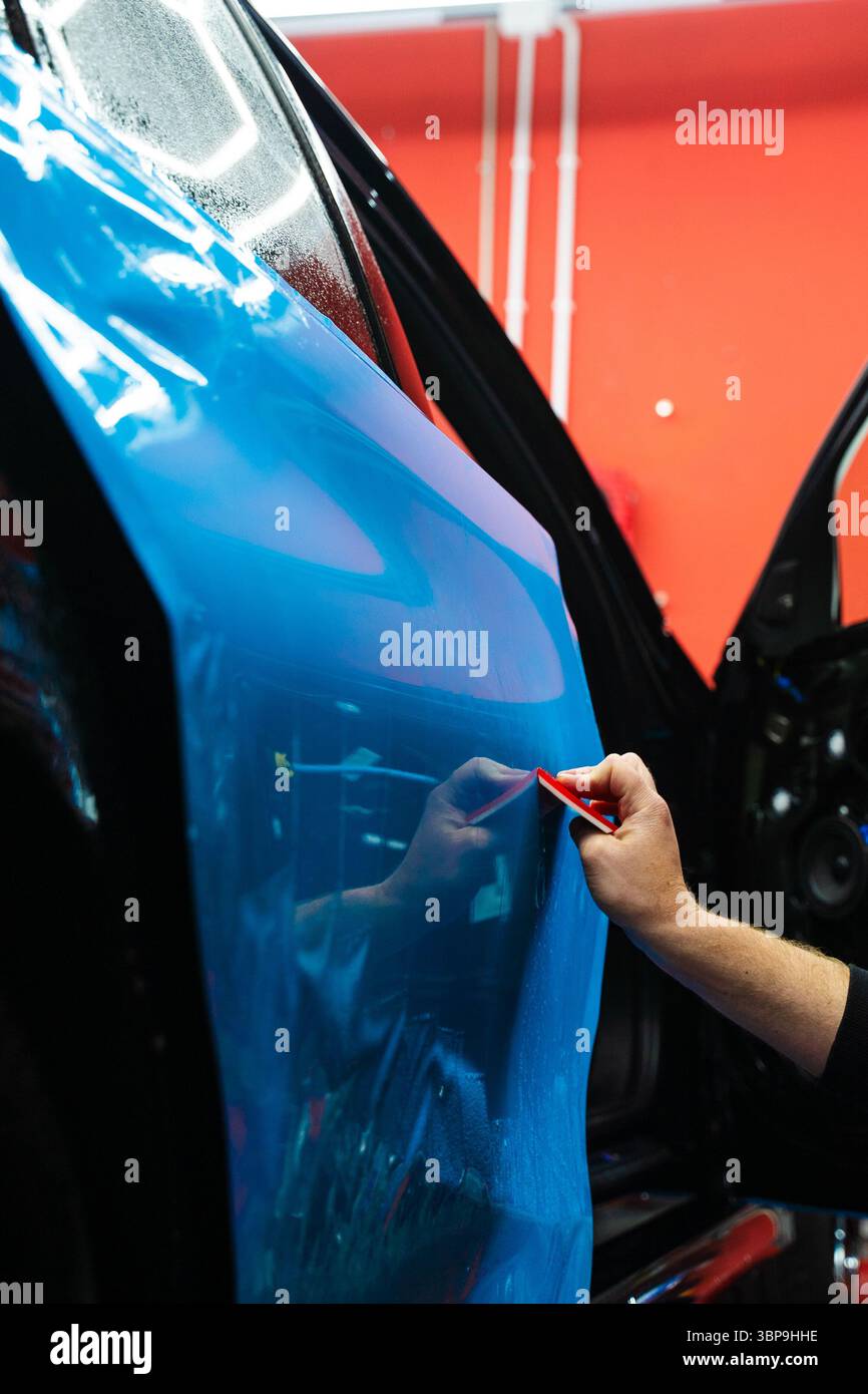 Detailing expert uses red squeegee wrapper to flatten blue PPF wrap on ...