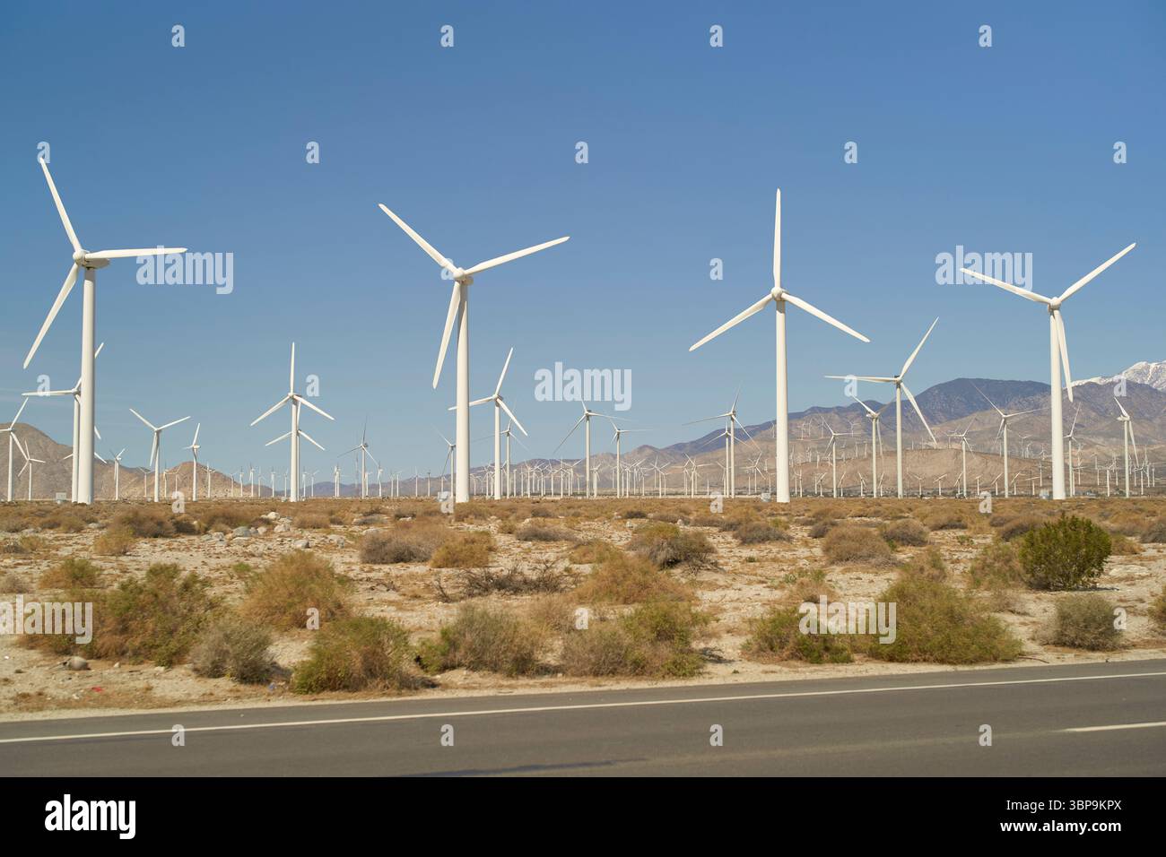 Wind turbines stand tall under a clear blue sky in a desert landscape ...