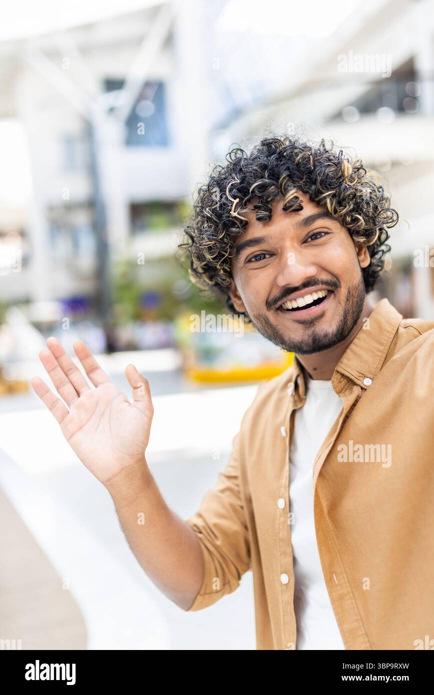 An attractive man waves hello in a video call using his phone, smiling ...