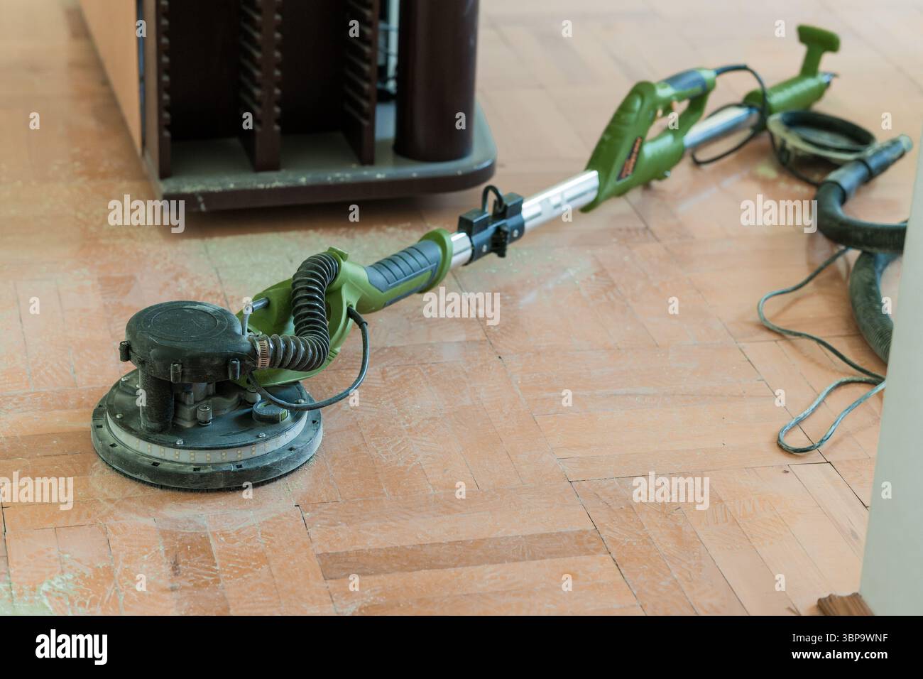 A green power sander is being used to refinish a wooden floor in a ...