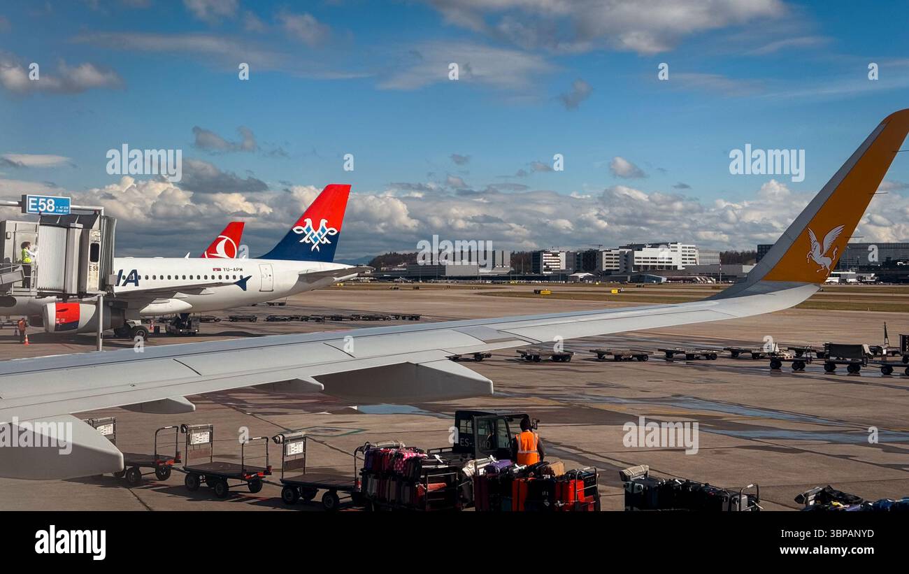Multiple planes are parked at Zurich airport, while ground crew loads ...