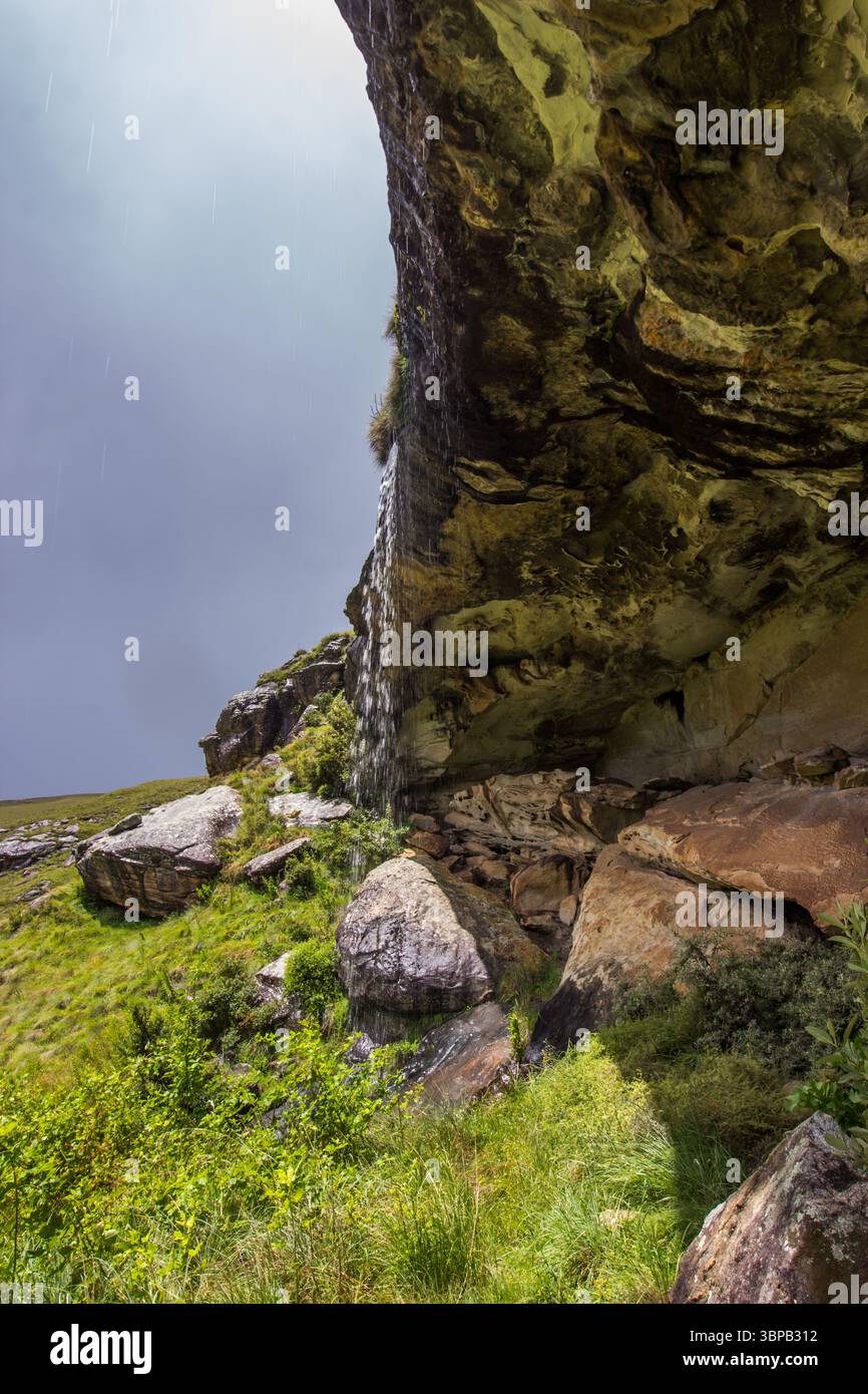 A small waterfall falling down a large sandstone overhang forming a ...