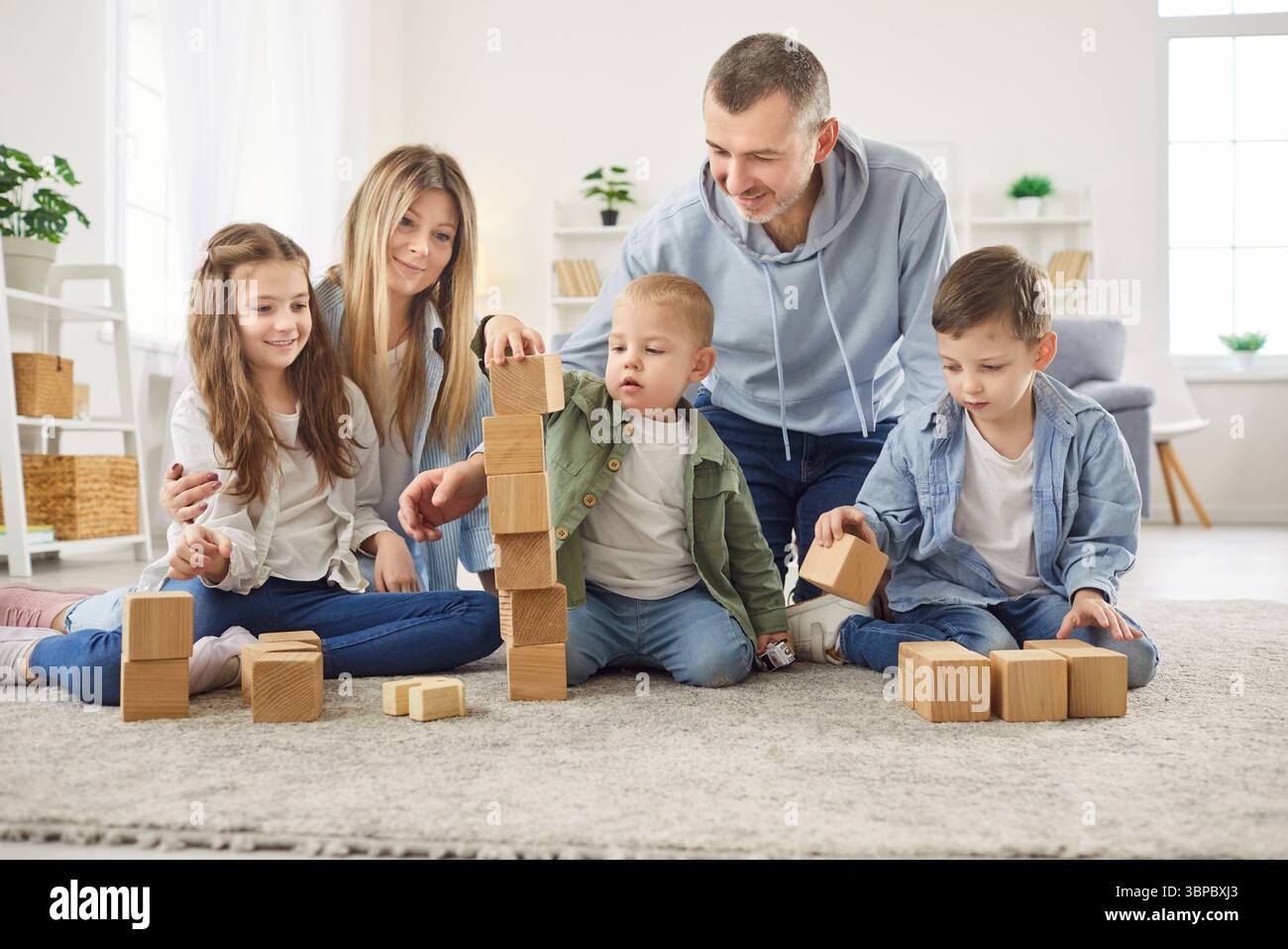Happy family sitting on carpet, building wooden block tower and ...