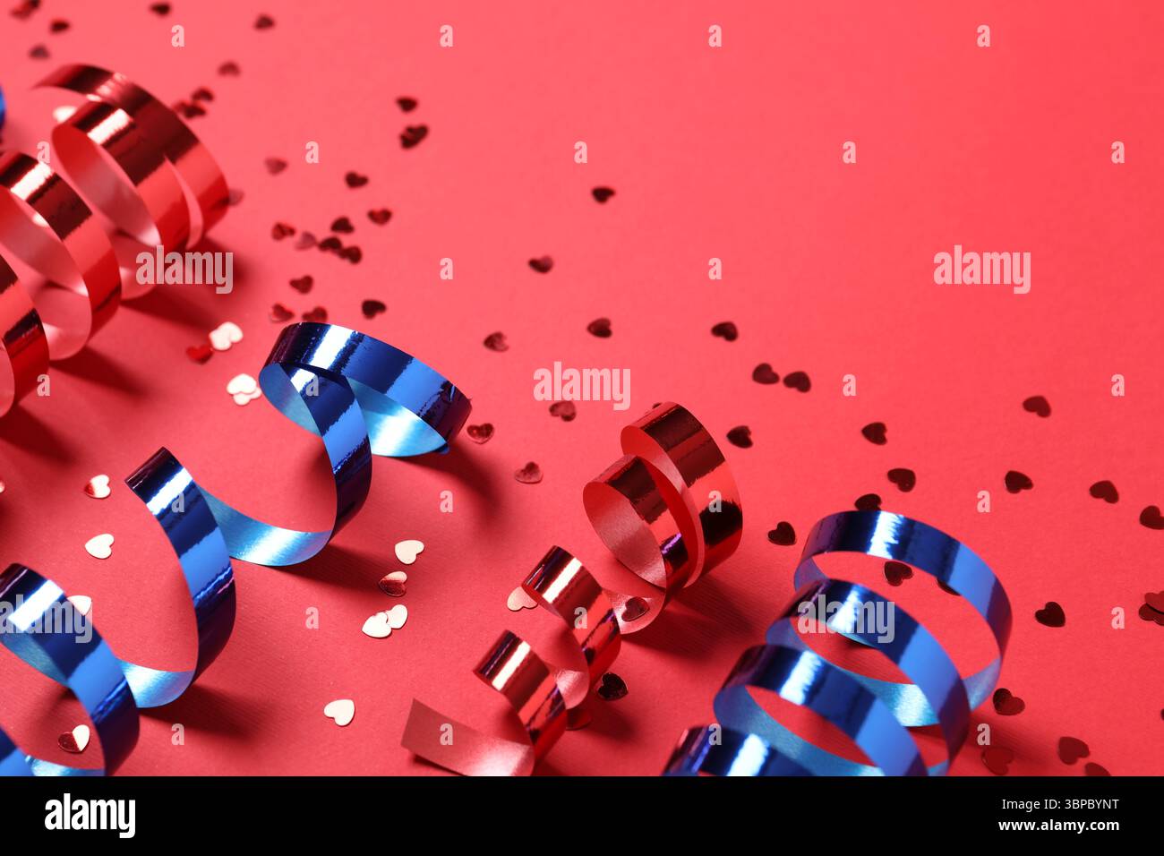 Shiny serpentine streamers and confetti on red background, above view ...