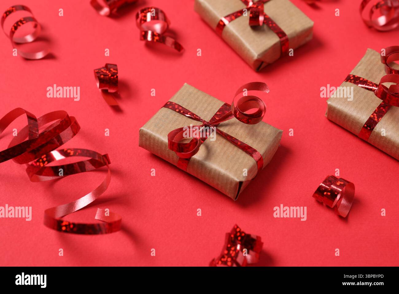 Shiny serpentine streamers and gift boxes on red background, above view ...