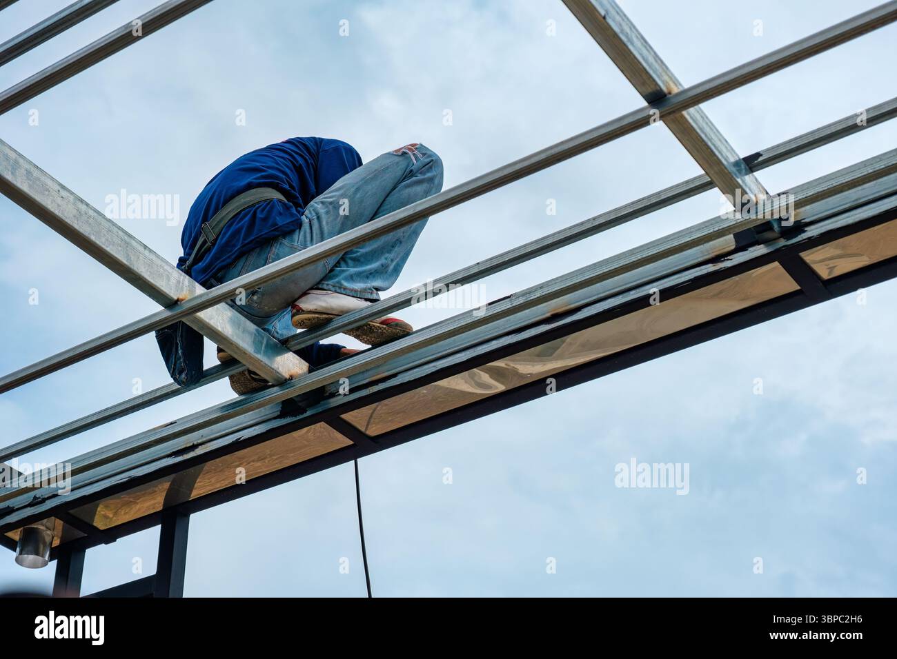 Construction worker installing and welding on steel frame of roof ...