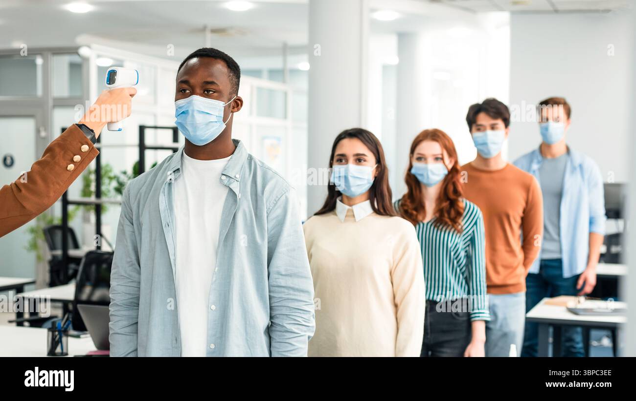 Woman with gun thermometer cheking diverse people temperature in line ...