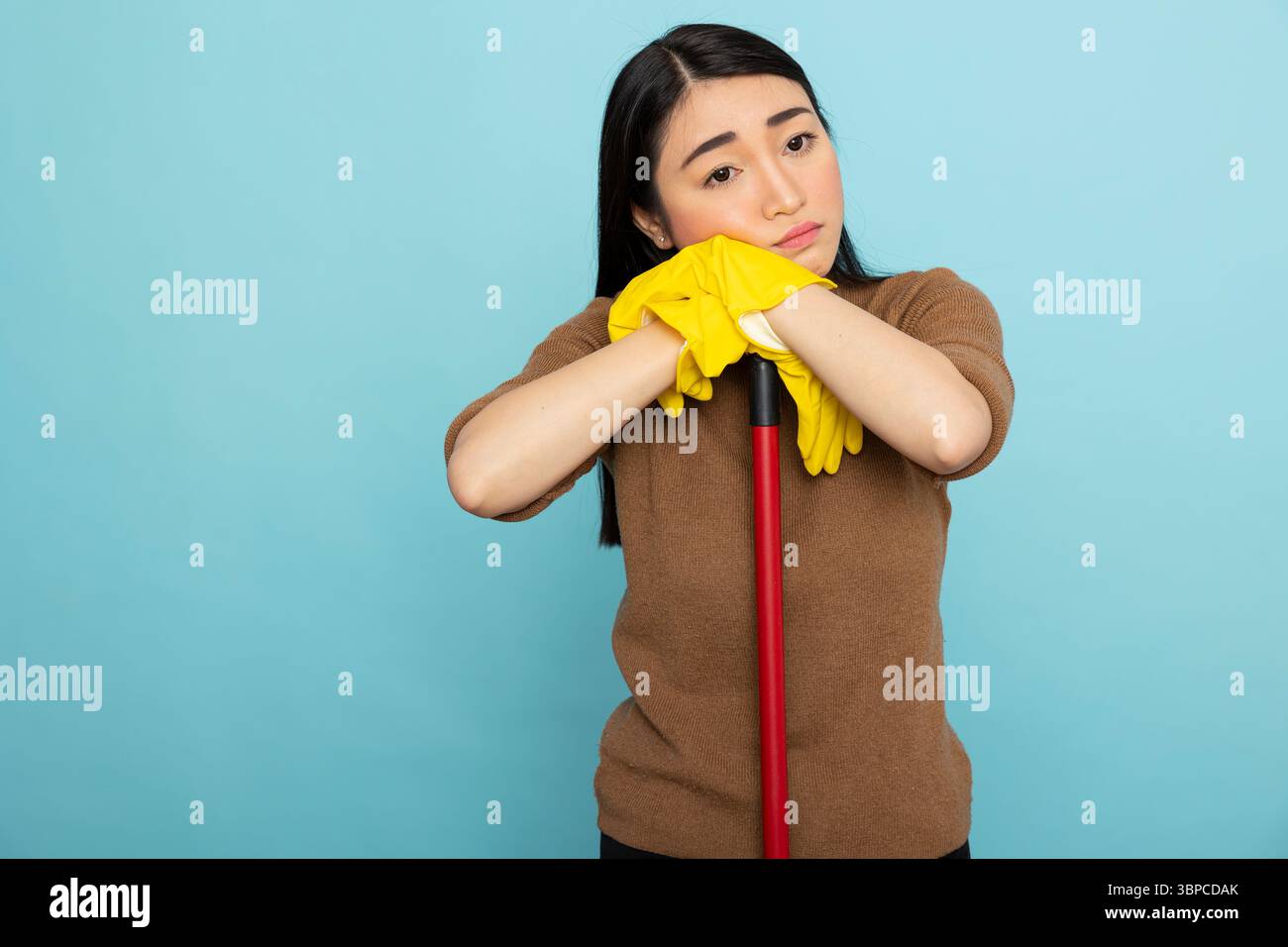 Exhausted asian female janitor leaning on broomstick, wearing yellow ...