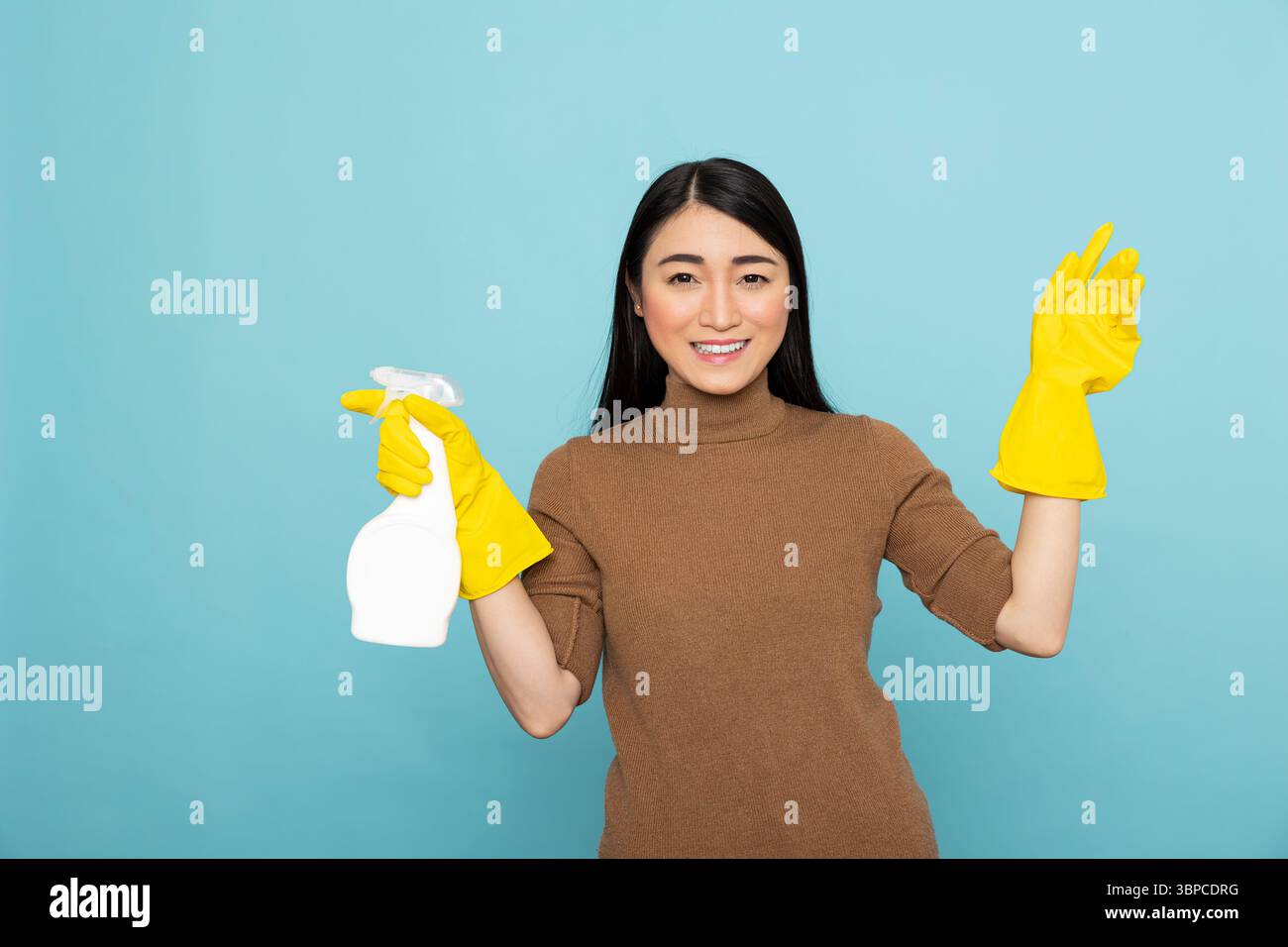 Joyful asian woman in rubber gloves lifts arms with cleaning spray in ...