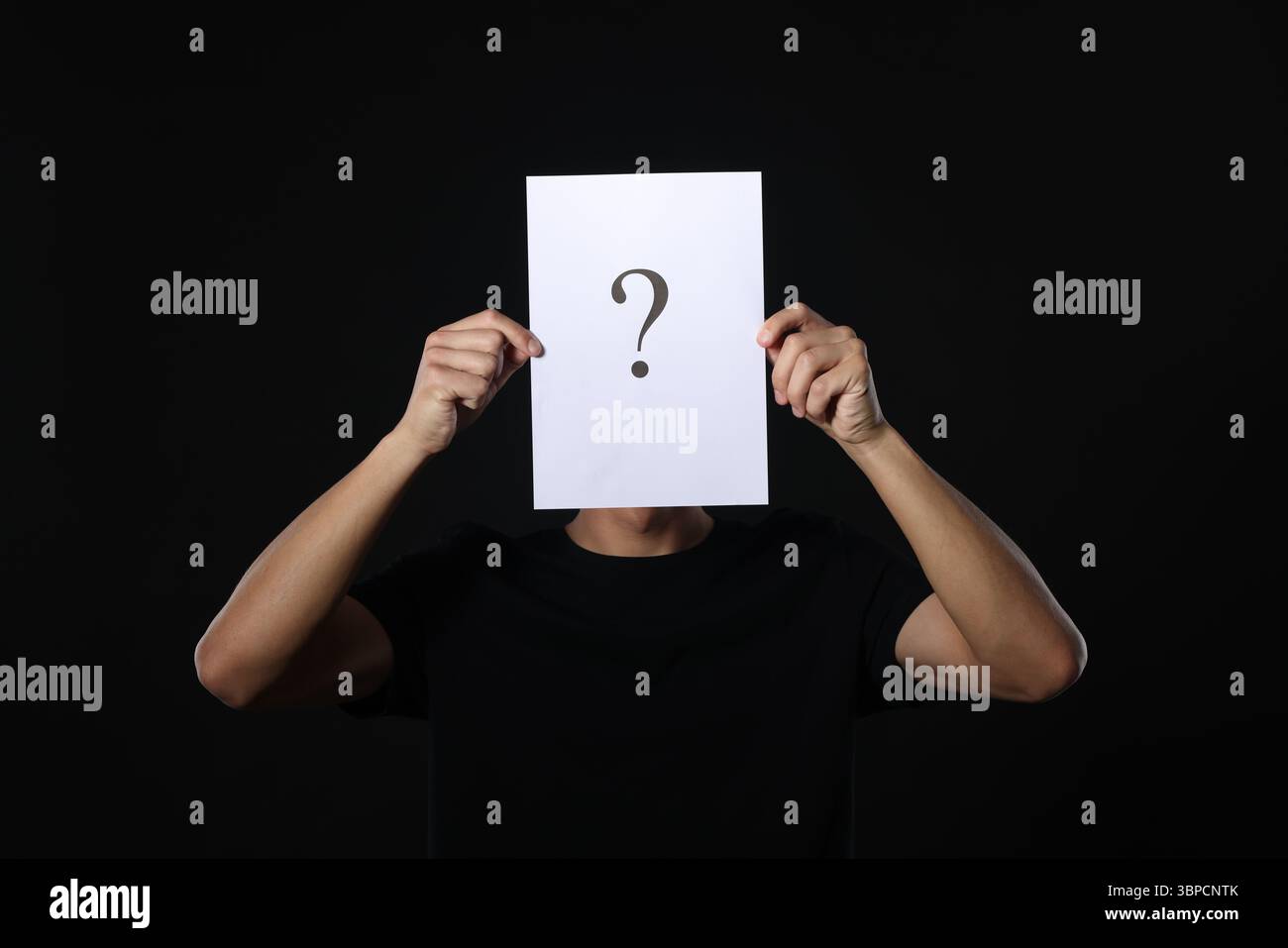 Man hiding behind paper sheet with question mark on dark background ...