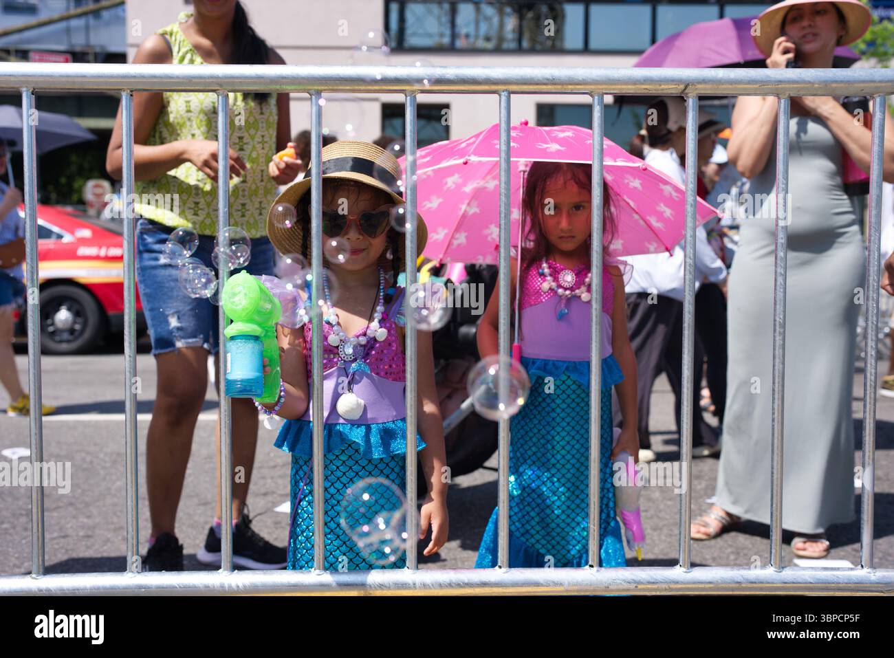 Two young girls in mermaid costumes, one holding a bubble blower, stand ...