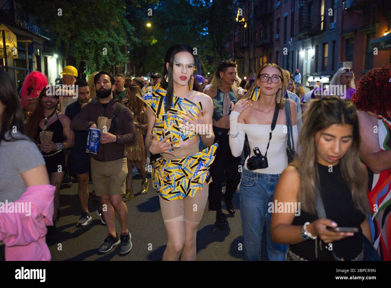 A nighttime street scene shows a diverse group of people, many in ...