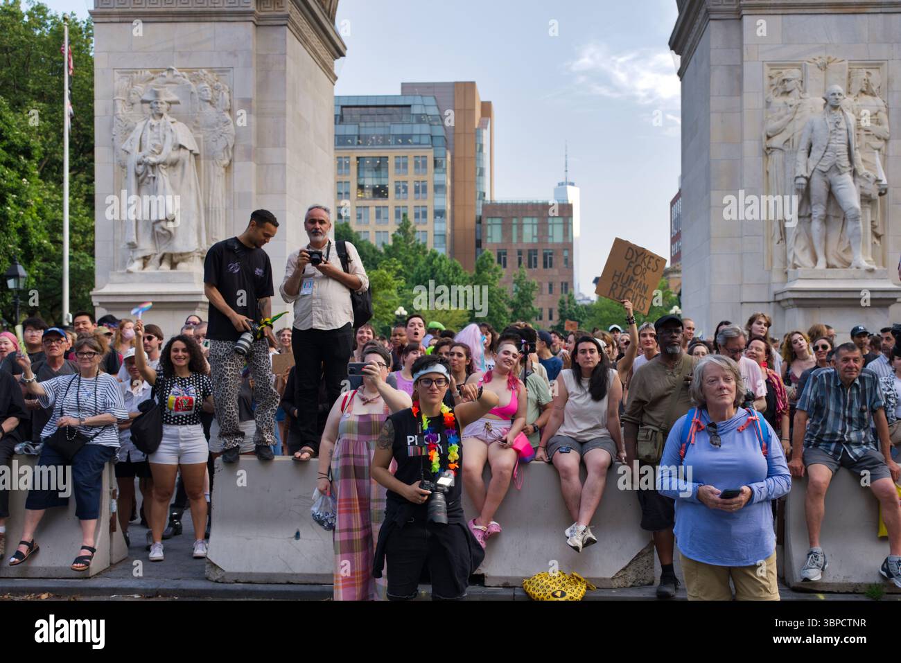 A crowd of diverse people, many holding signs, are gathered at a stone ...