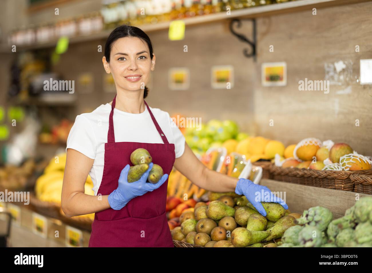 Adult female seller putting pears in vegetable shop Stock Photo - Alamy