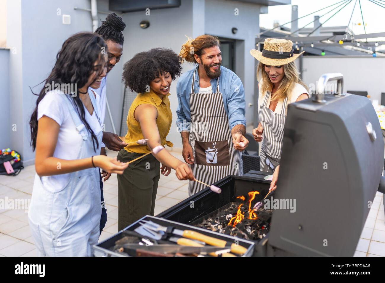 Happy friends enjoying a rooftop party, roasting marshmallows over a ...