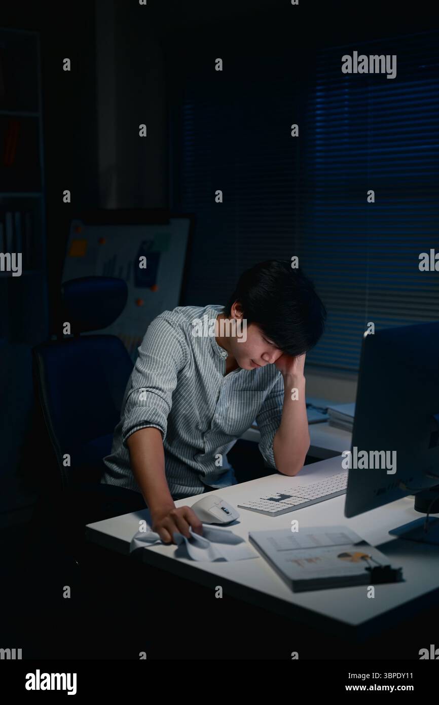 Man working late at night in a dim office, showing signs of stress and ...