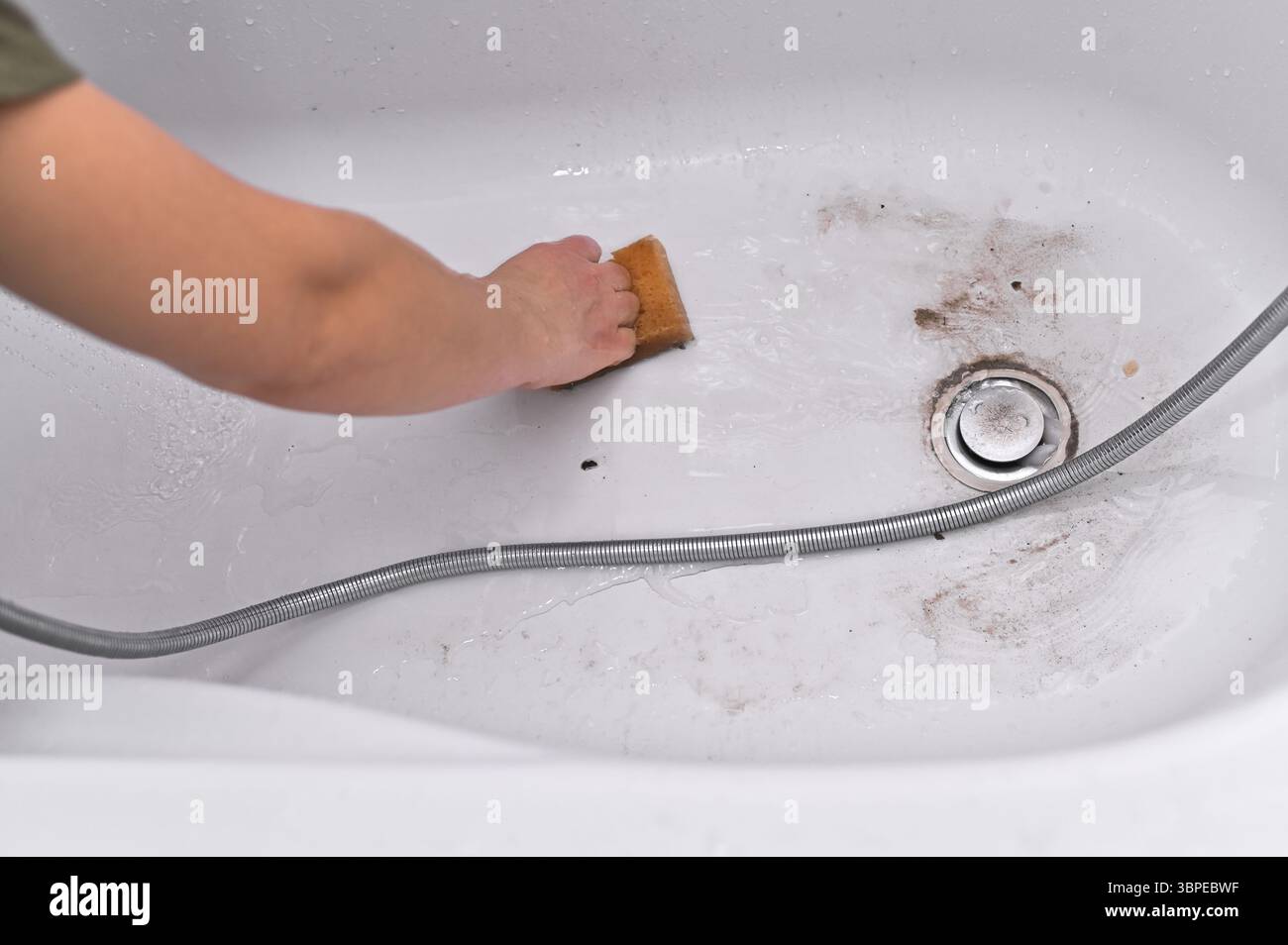 Hand uses sponge to scrub dirty bathtub surface with visible stains ...