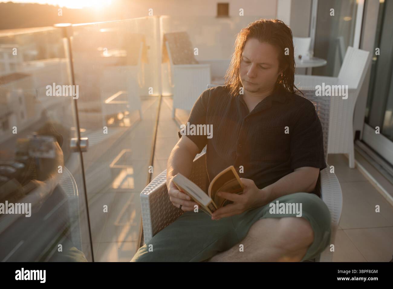 Man with wet hair reading book during golden hour relaxed posture ...