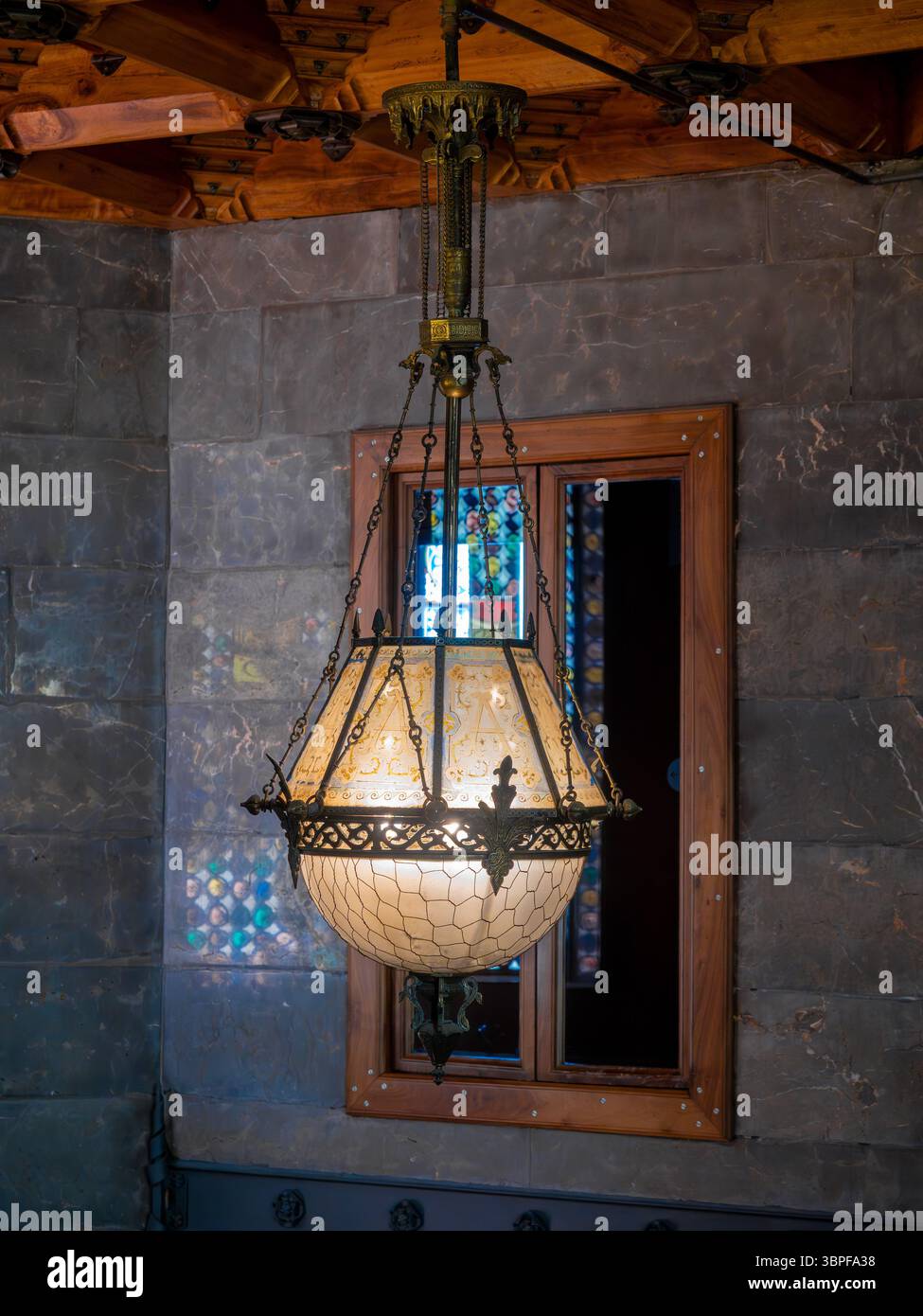 Close-up of an ornate Art Nouveau lamp against a stone wall and window ...