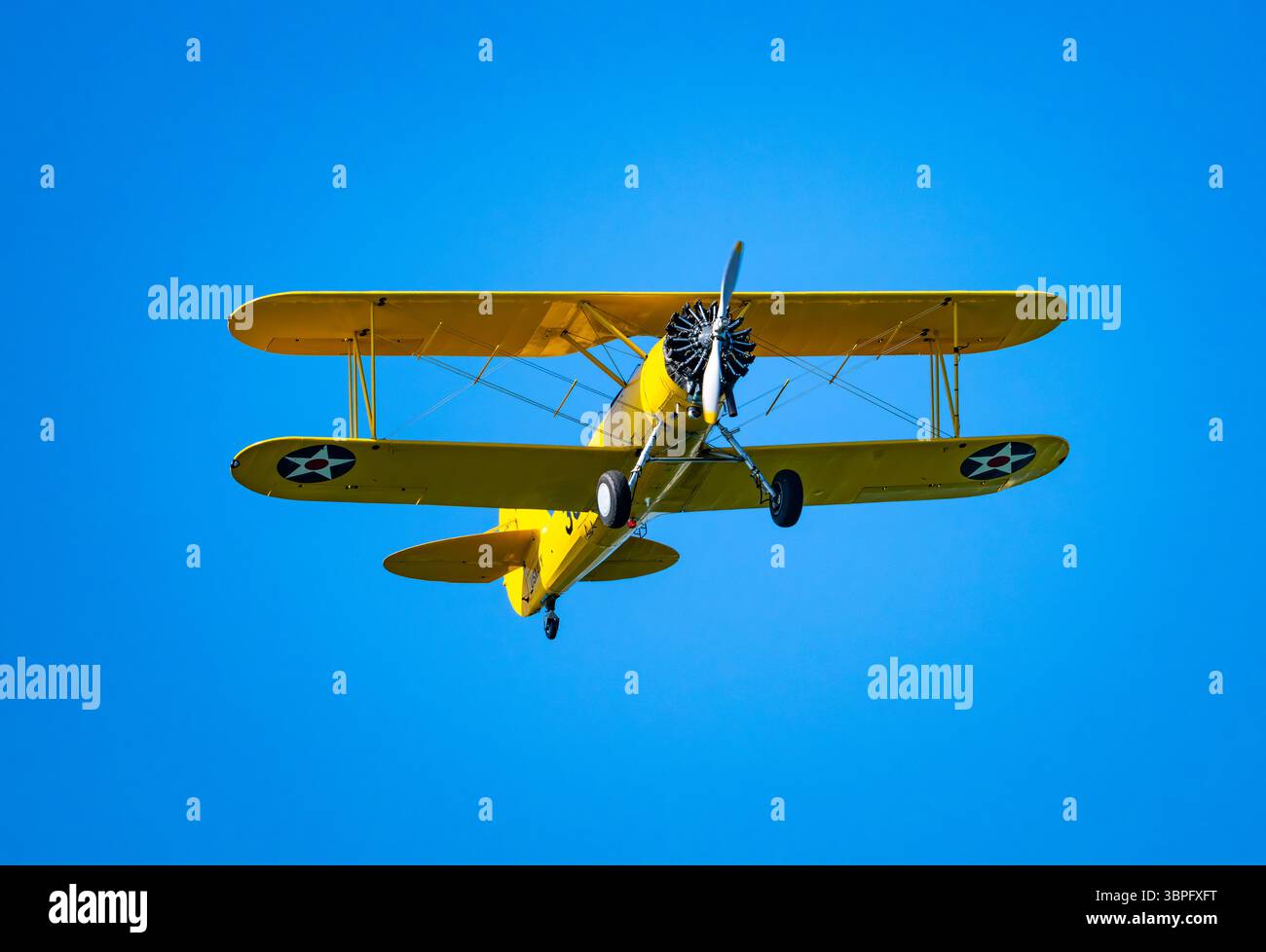 A bright yellow Boeing Stearman biplane flying in blue sky. California ...