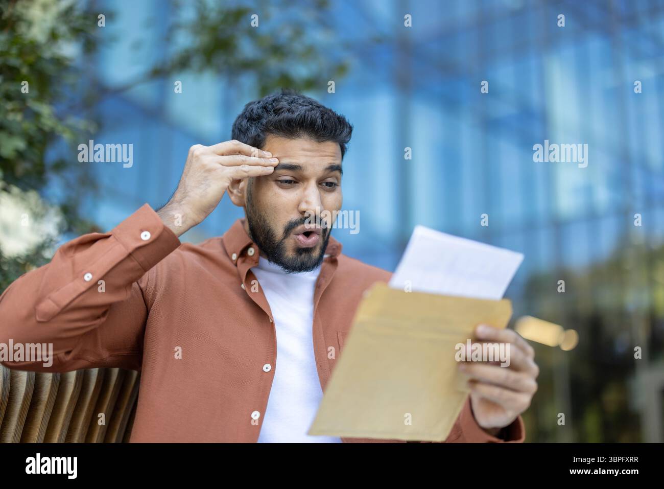 An Indian man reacts with shock while reading a letter outdoors ...