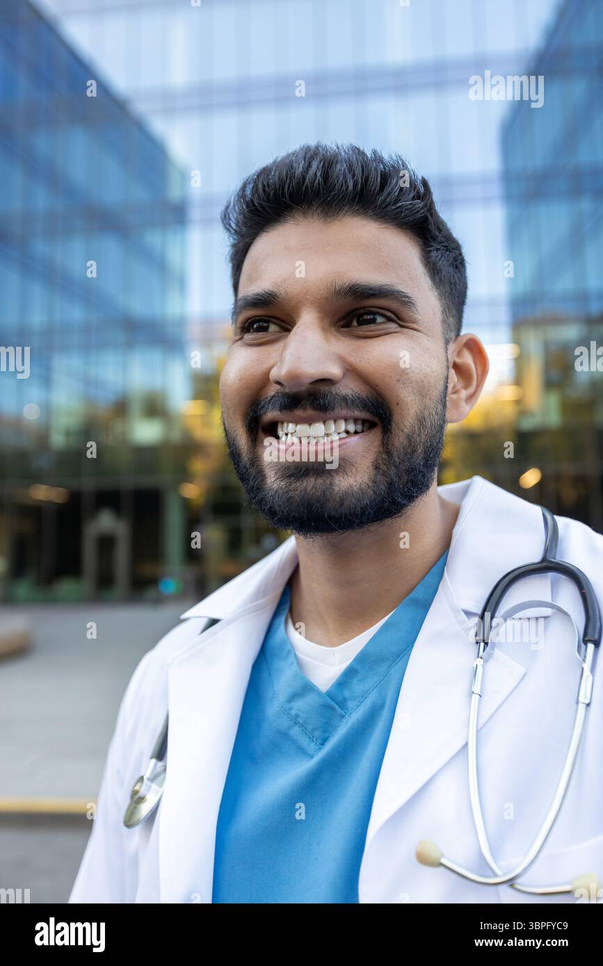 A smiling male doctor with a stethoscope looks away from the camera ...