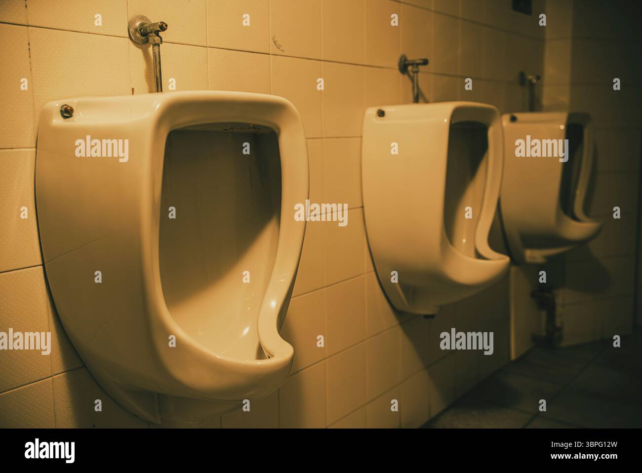 Three white ceramic urinals aligned on a tiled wall in a public ...