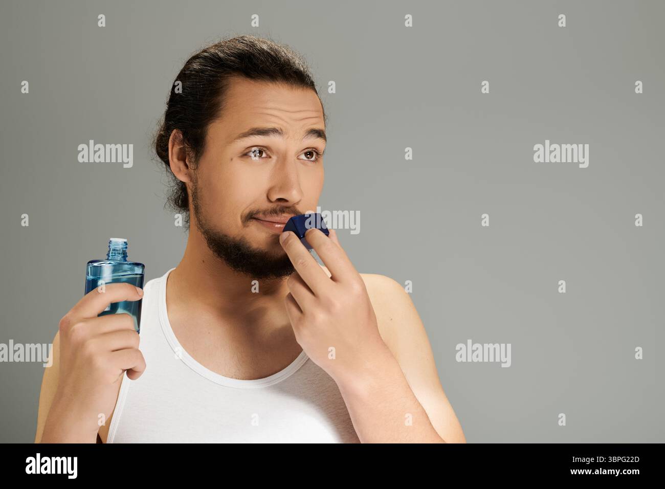 Charming young man with a beard considers fragrance application while ...