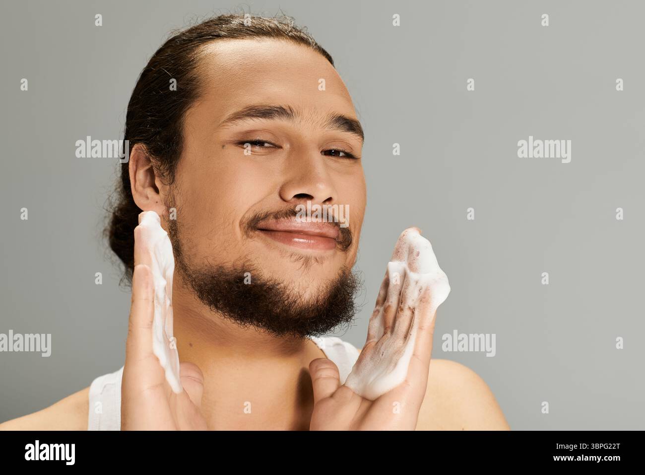 Bearded young man happily cleansing his face with a foamy wash ...