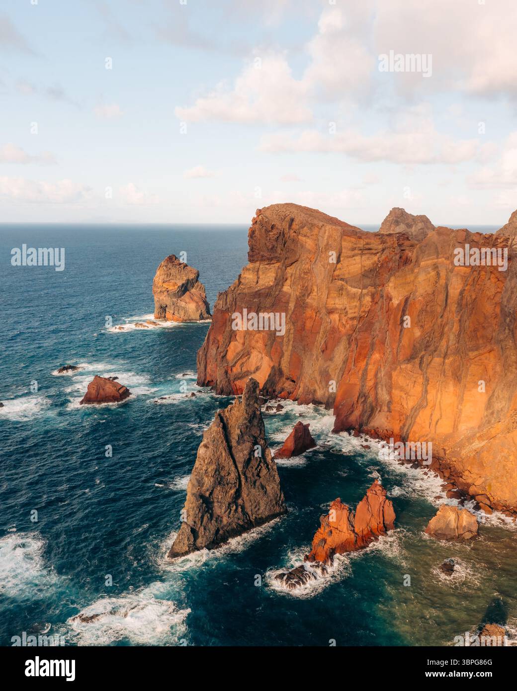 Aerial view of rugged cliffs ablaze with warm light meet the churning ...