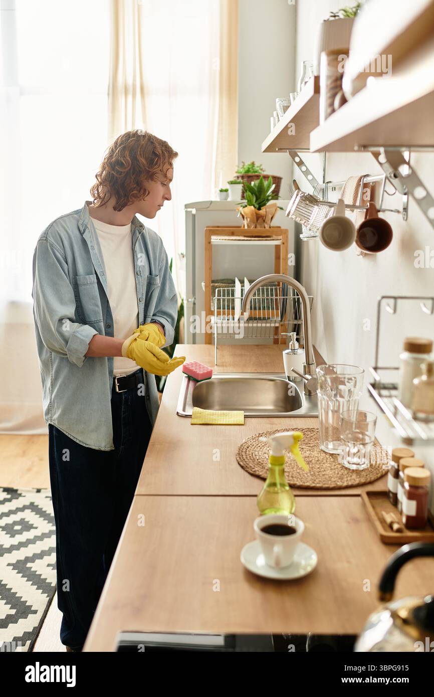 A handsome young man is focused on cleaning the kitchen sink at home ...