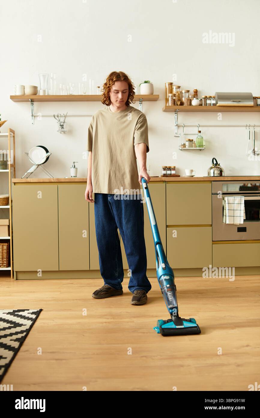 Stylish young man tidying up his cozy kitchen while operating a vacuum ...