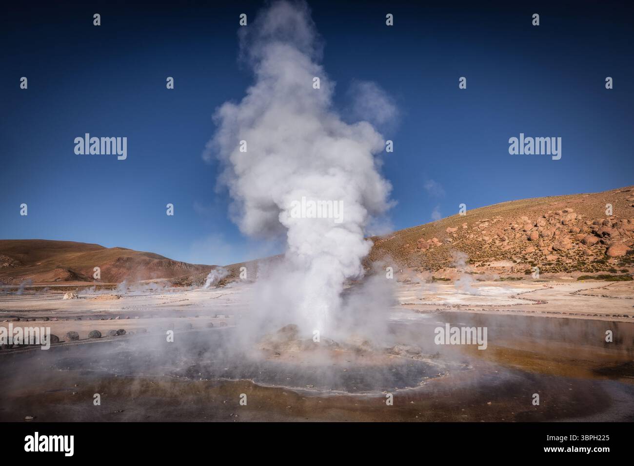 View of rising steam from a geyser against a backdrop of arid, sun ...