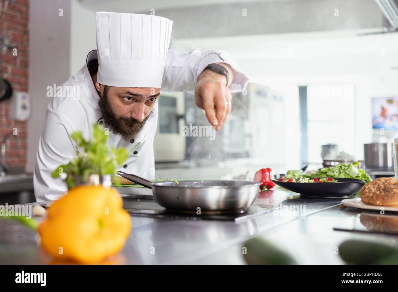 Head chef in restaurant kitchen adds a final touch of herbs to plated ...