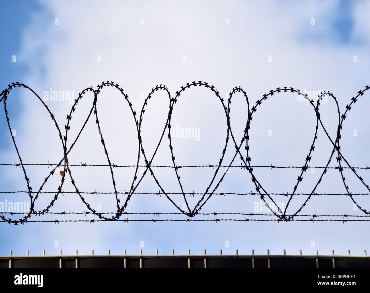 Barbed wire on a background of blue sky with white clouds. The concept ...