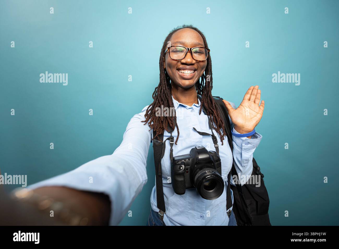 Black female vlogger with dslr around neck waves at camera, recording ...